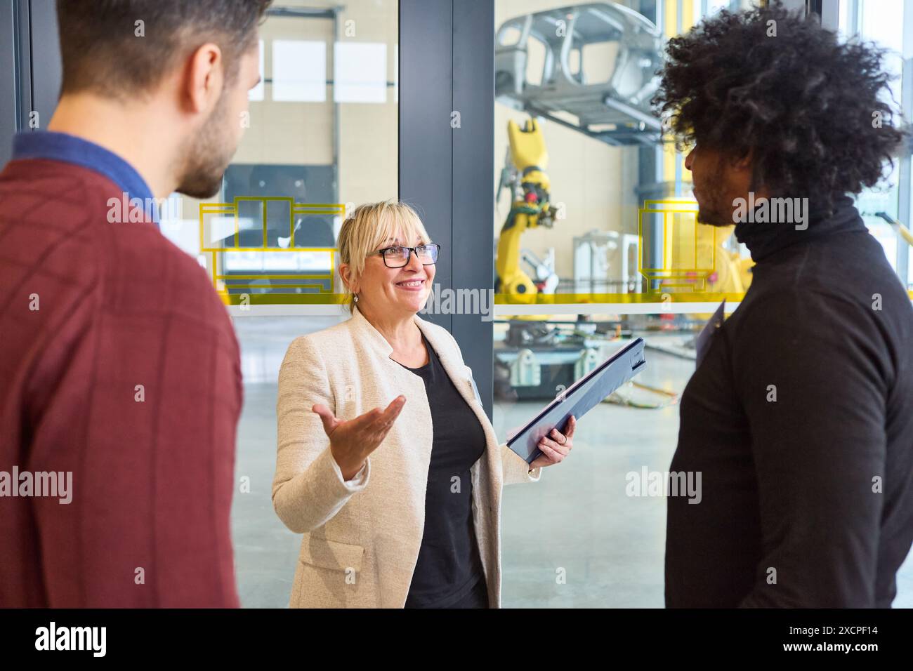 Three people discussing robotics and automation in an industrial setting. Technological ...