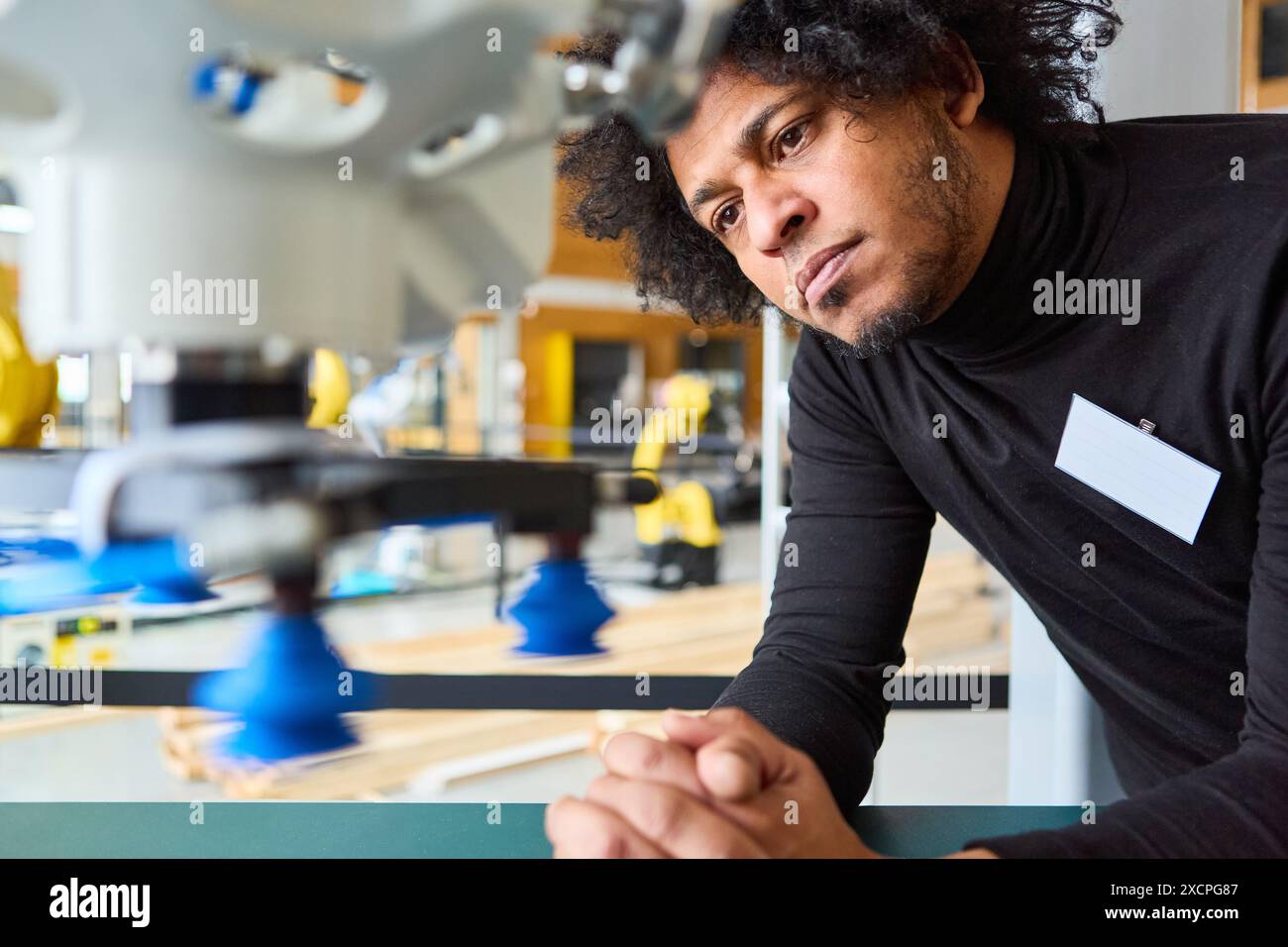 Engineer Attentively Watching A Robotic Gripper Arm In An Industrial Environment Highlighting