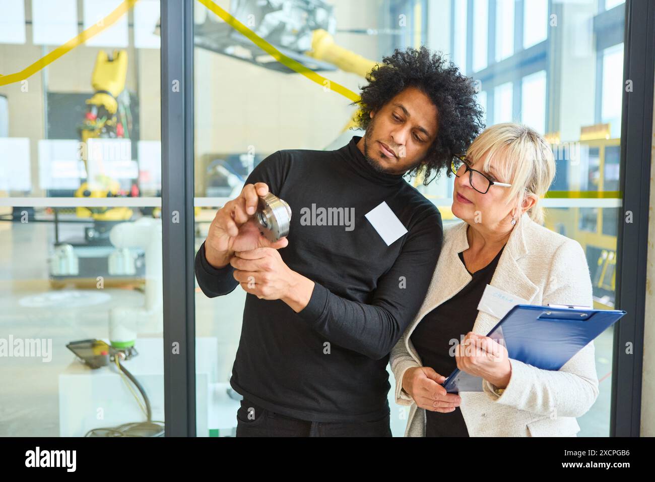 Two Engineers Closely Examine A Robotic Gripper Part In An Industrial Setting Emphasizing