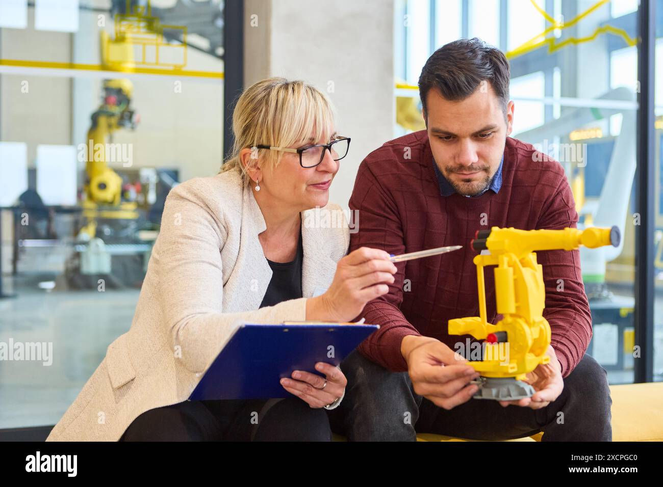 Two engineers collaborating on the design and functionality of a robotic arm in an industrial ...