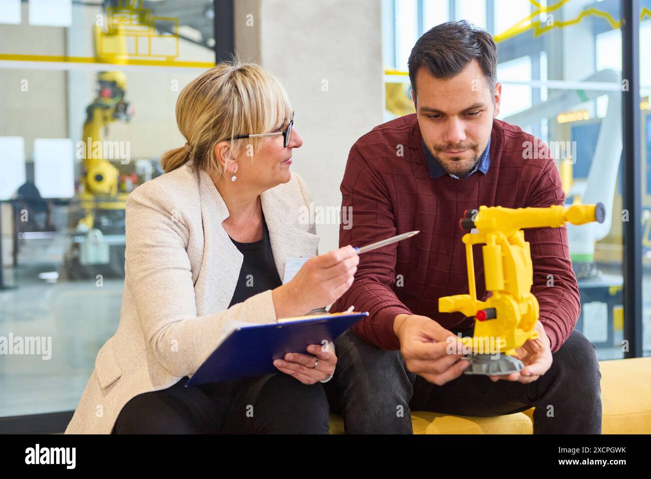 Two engineers discussing the development of a robotic gripper arm in a ...