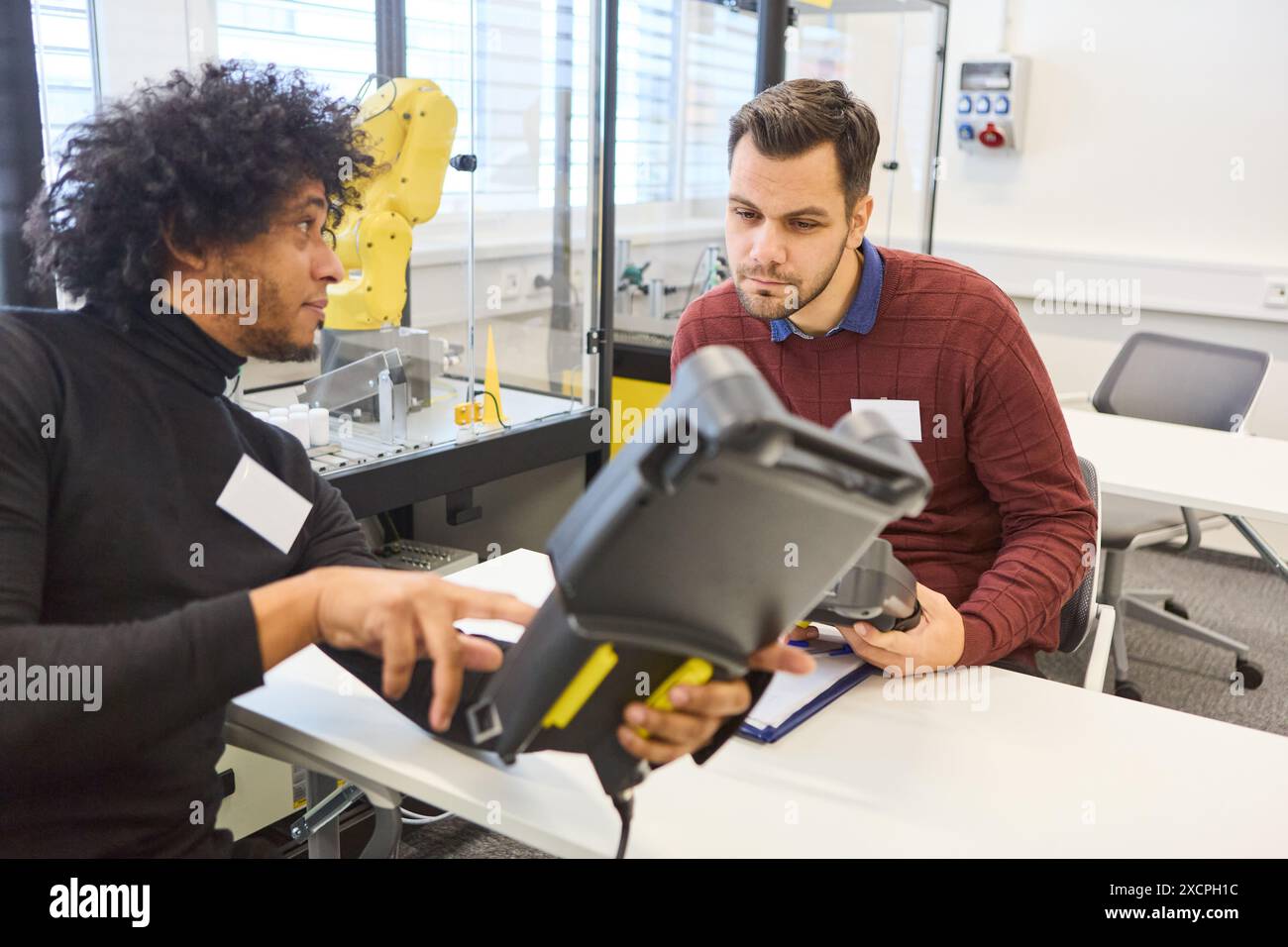 Two engineers engaged in programming and controlling a robotic arm in a ...
