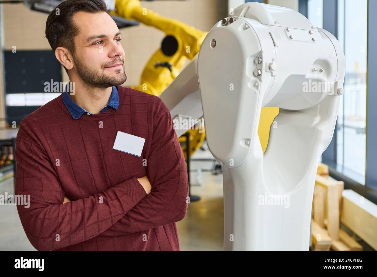 Engineer with folded arms standing beside a robotic arm in a modern ... Engineer with folded arms standing beside a robotic arm in a modern ...