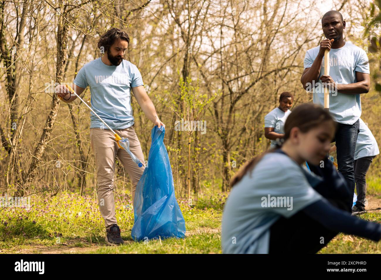 Diverse activists picking up garbage and plastic trash with tongs ...