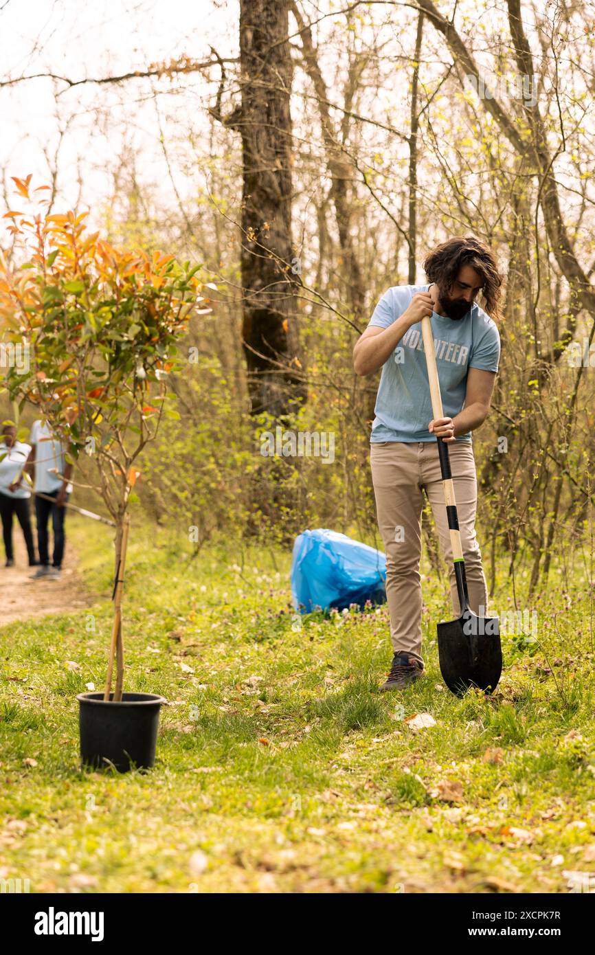 Young man volunteer using a shovel to dig holes in the ground, planting ...