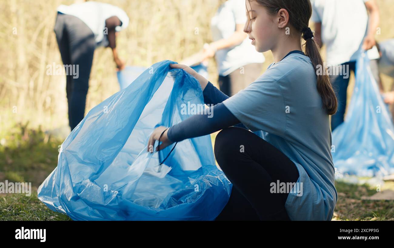 Tired little girl collecting trash and plastic bottles from the forest ...