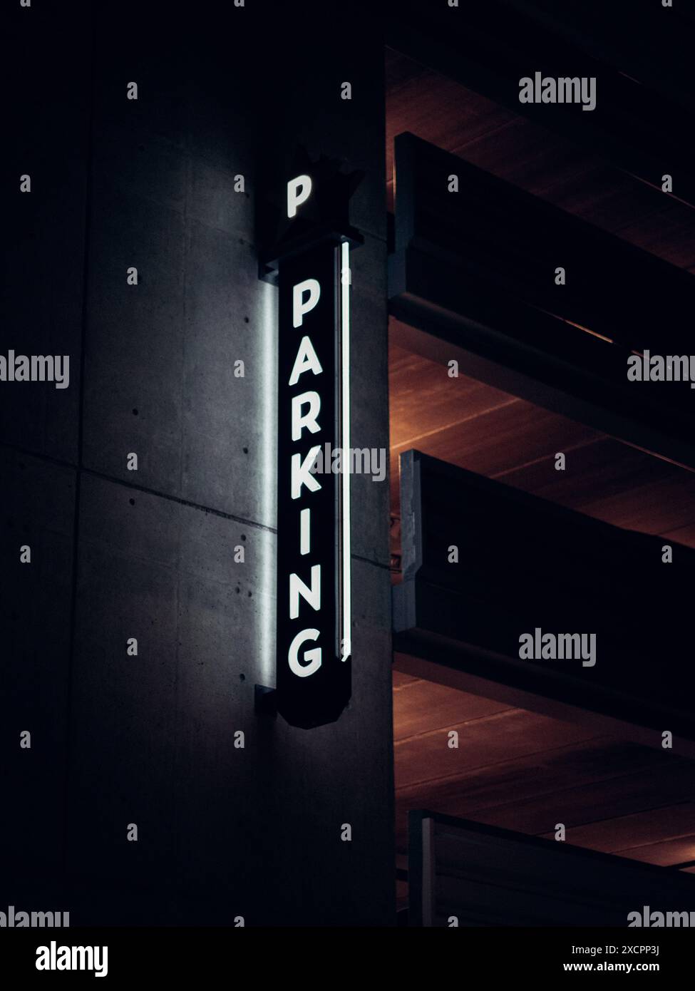 A neon parking sign illuminated at night on a concrete wall of a ...