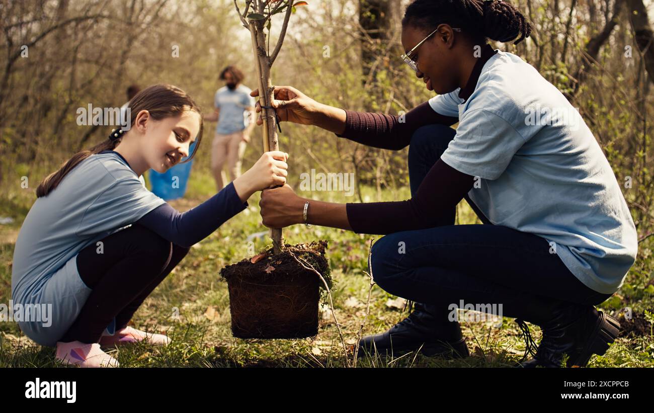 Two diverse girls do voluntary work by planting small trees in the ...