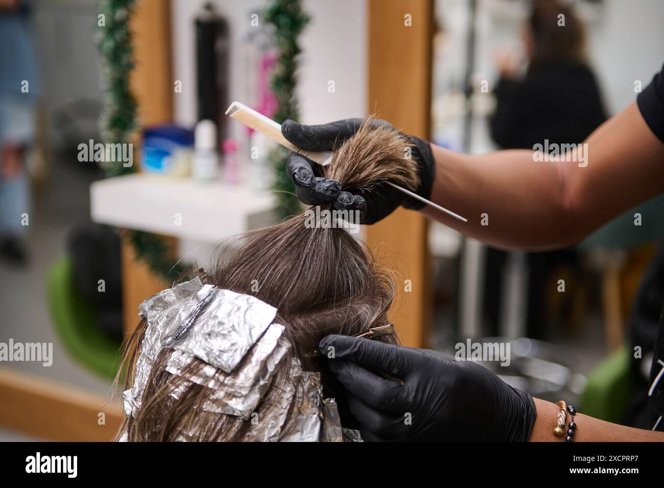 A hairdresser wearing gloves applies highlights to a client's hair ...