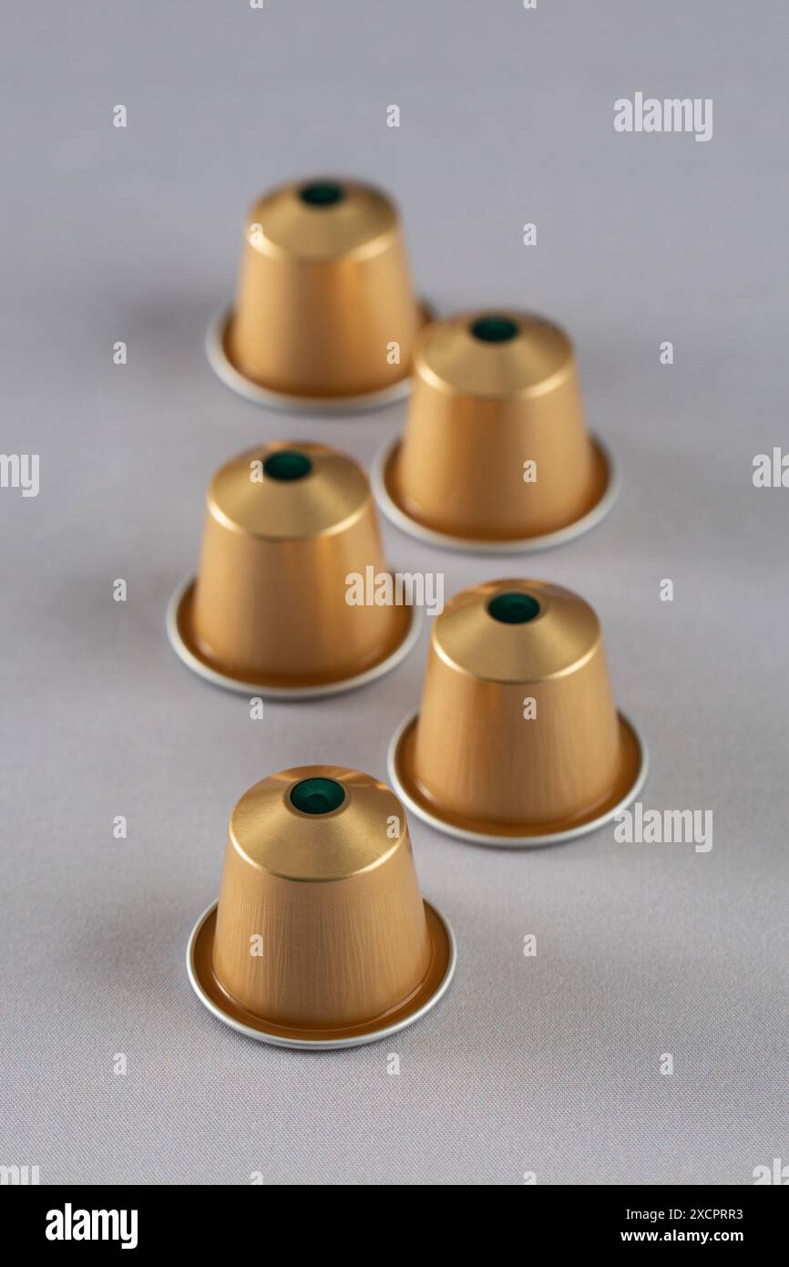 Five gold coffee capsules arranged on a neutral background, modern ...