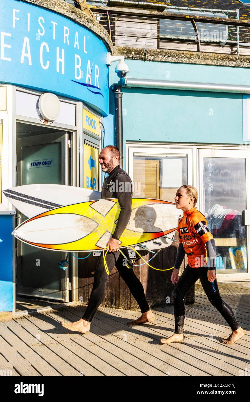 A father and son carrying surfboards and walking past the Fistral Beach ...