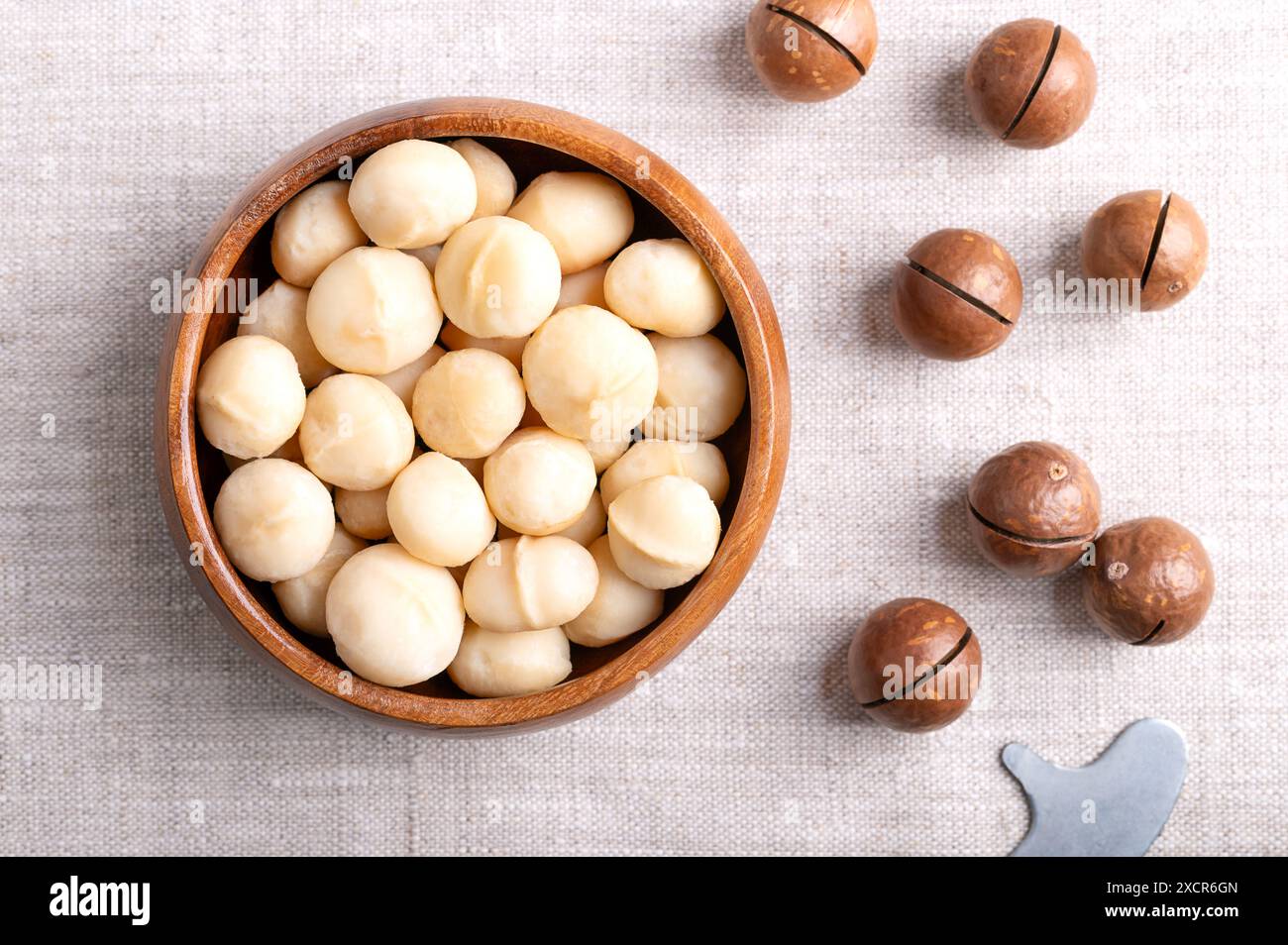 Roasted macadamia nuts in a wooden bowl on linen fabric. On the right ...