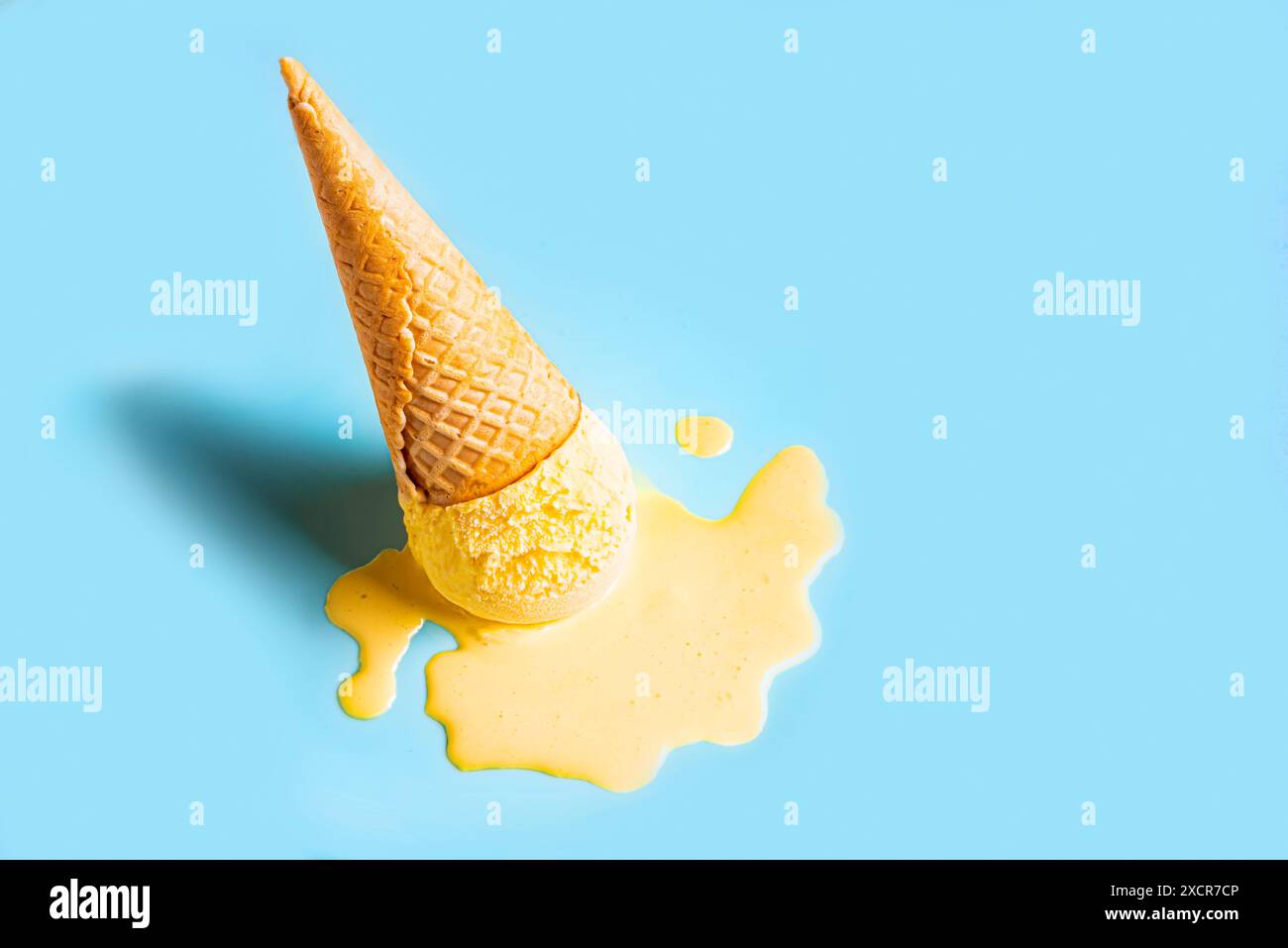 Yellow ice cream melting and spilling in waffle cone on pastel blue ...