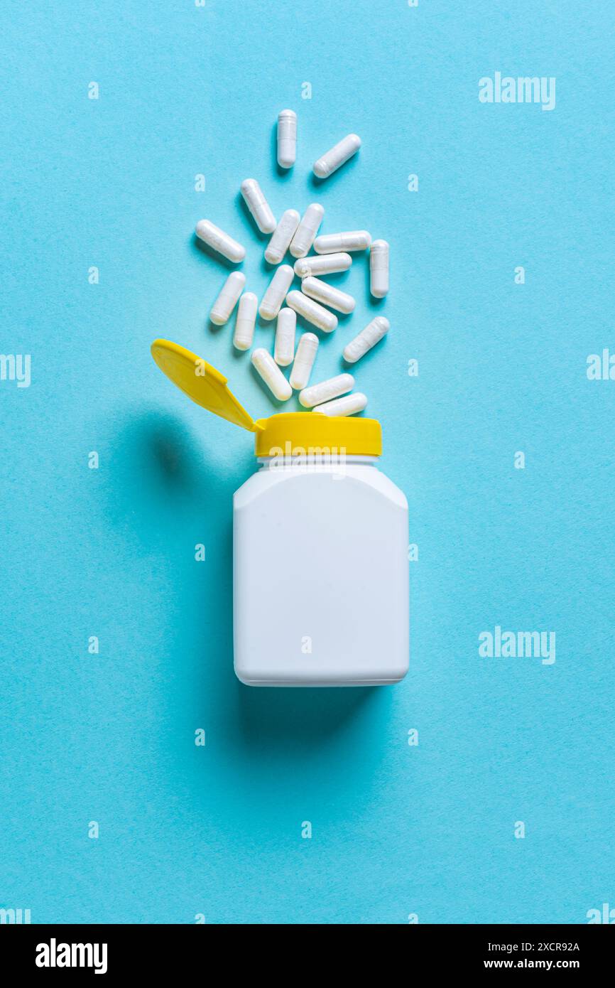 White capsules, dietary supplements in plastic bottle on blue ...