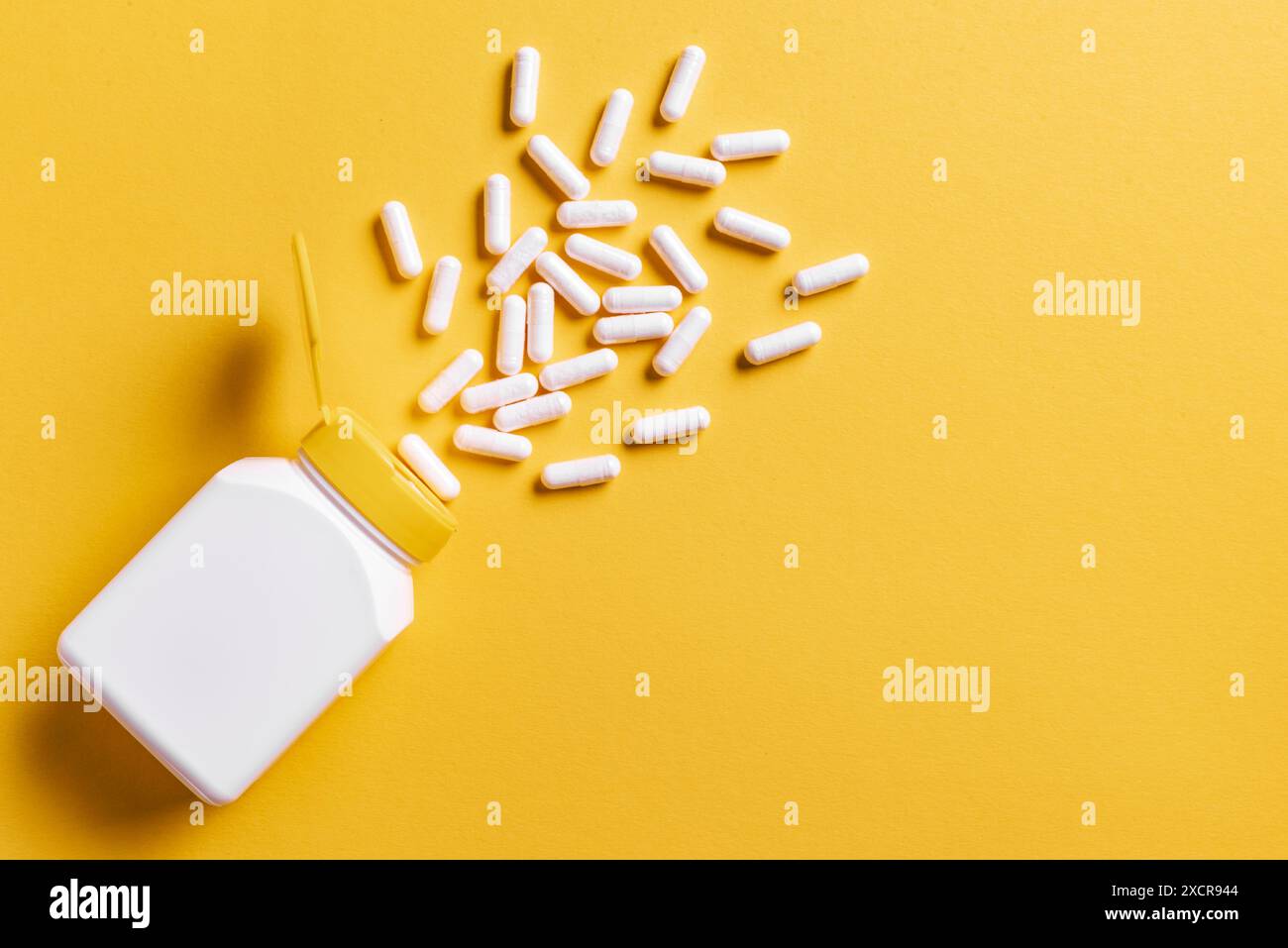 White supplement capsules in plastic bottle on bright yellow background ...