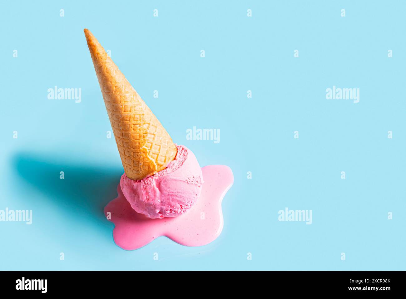 Pink ice cream melting and spilling from the waffle cone on pastel blue ...