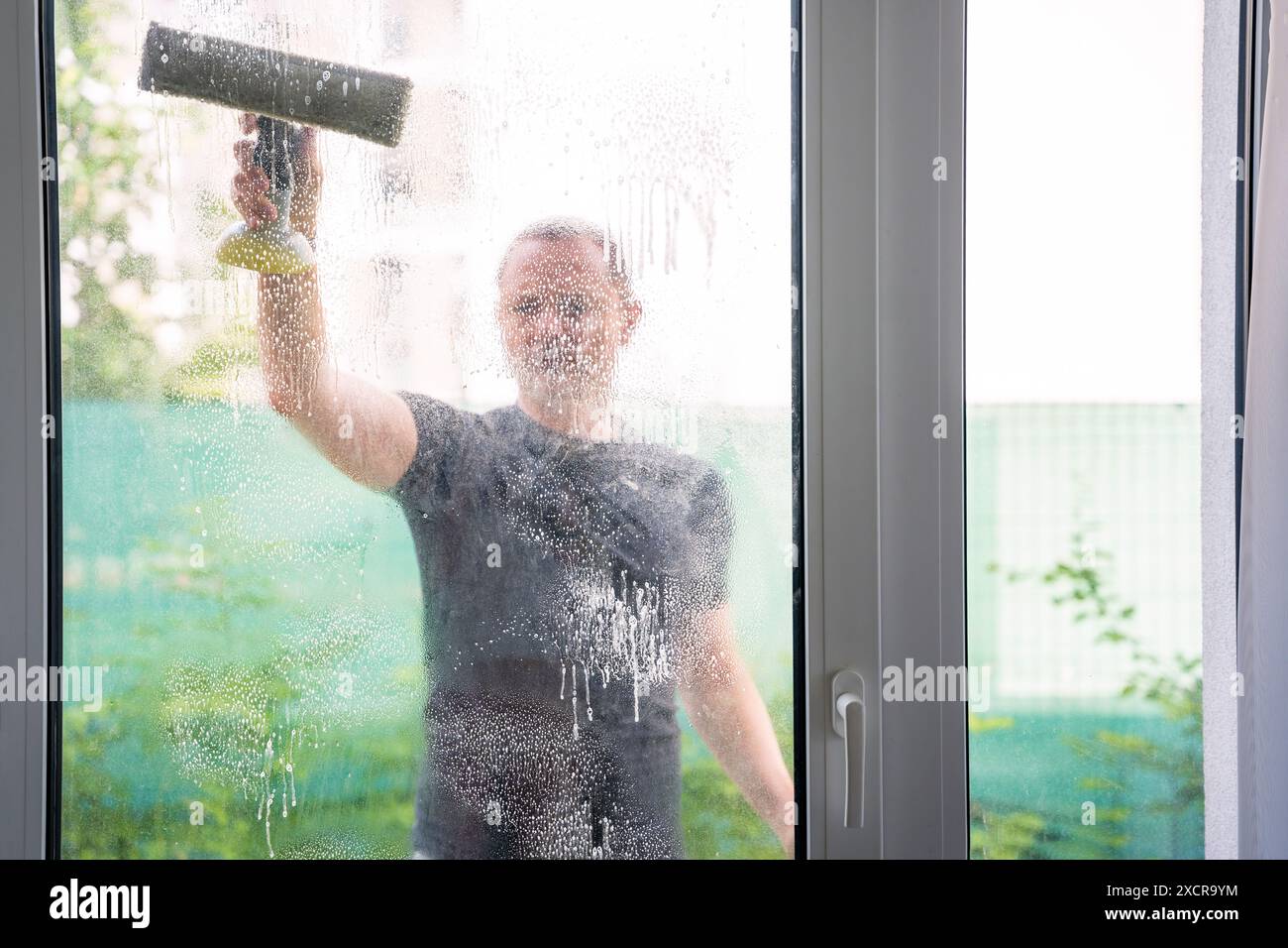Young man cleans the windows in the house. He splashes detergent, rubs ...