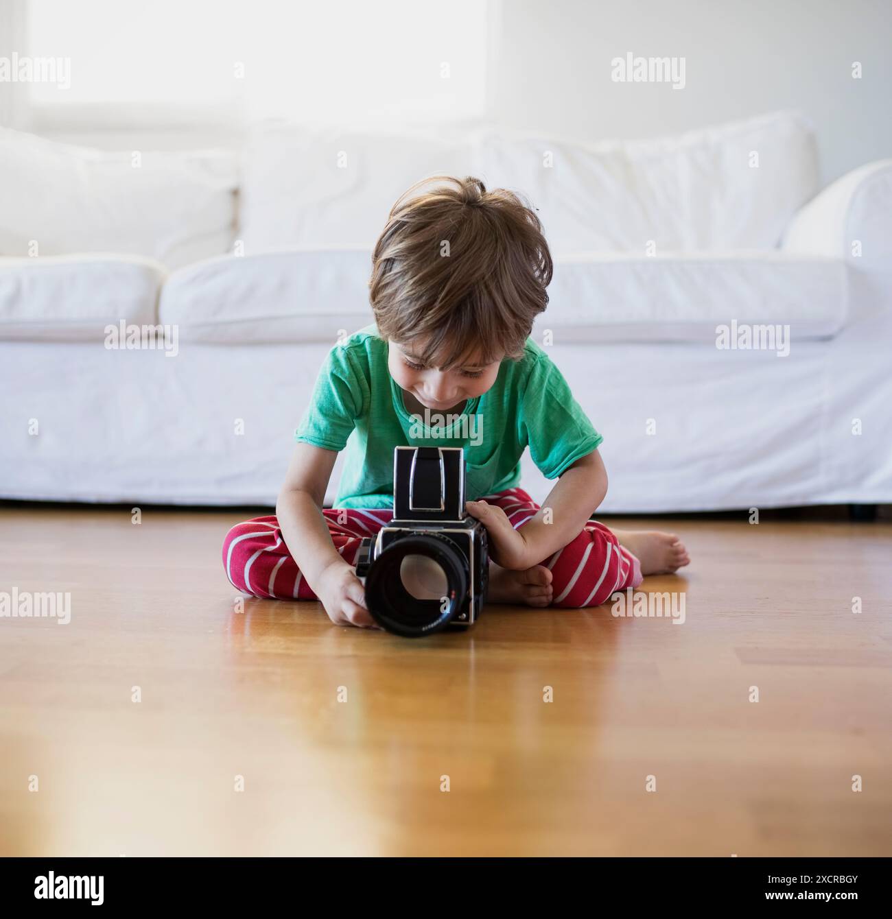 A young boy in a sunny room studies a vintage camera with curiosity ...