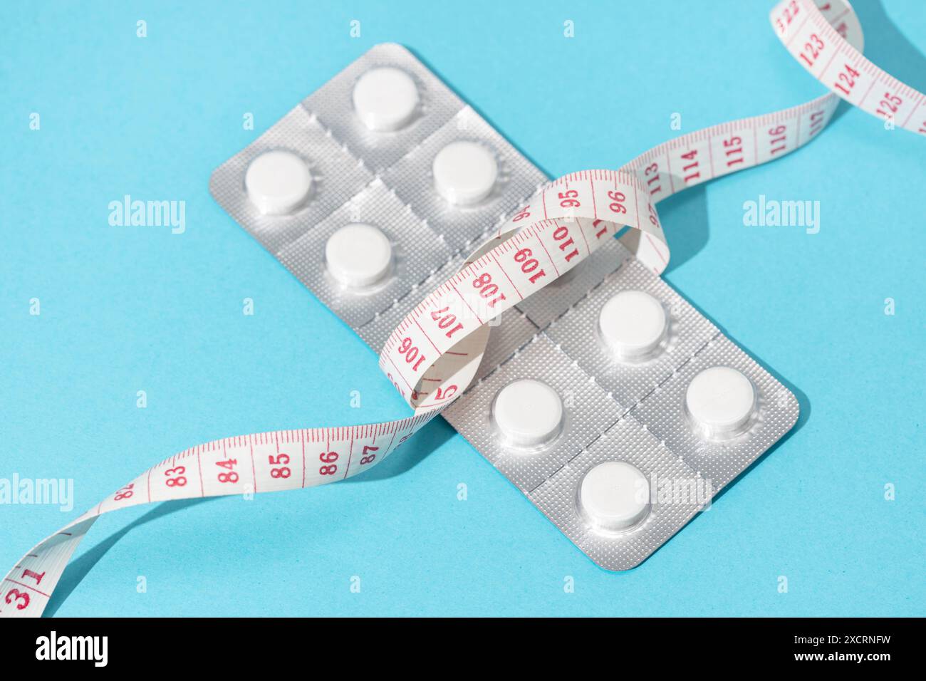 Measuring tape wrapped around a tablet blister pack on blue background ...