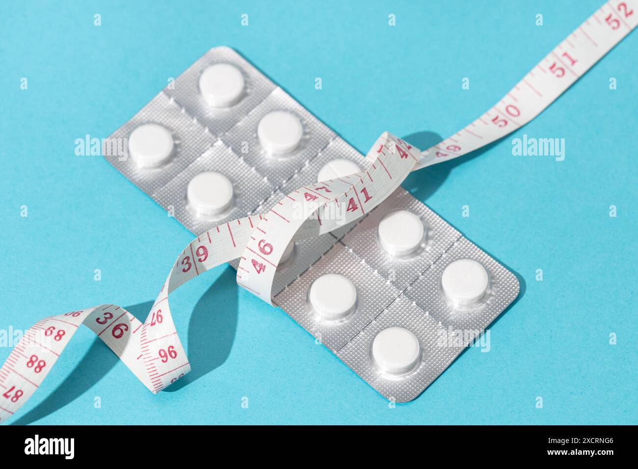 Measuring tape wrapped around a tablet blister pack on blue background ...