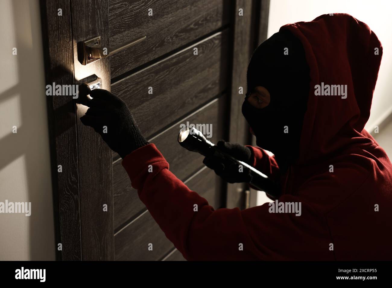 Thief with flashlight breaking foreign door's lock in hall. Burglary ...