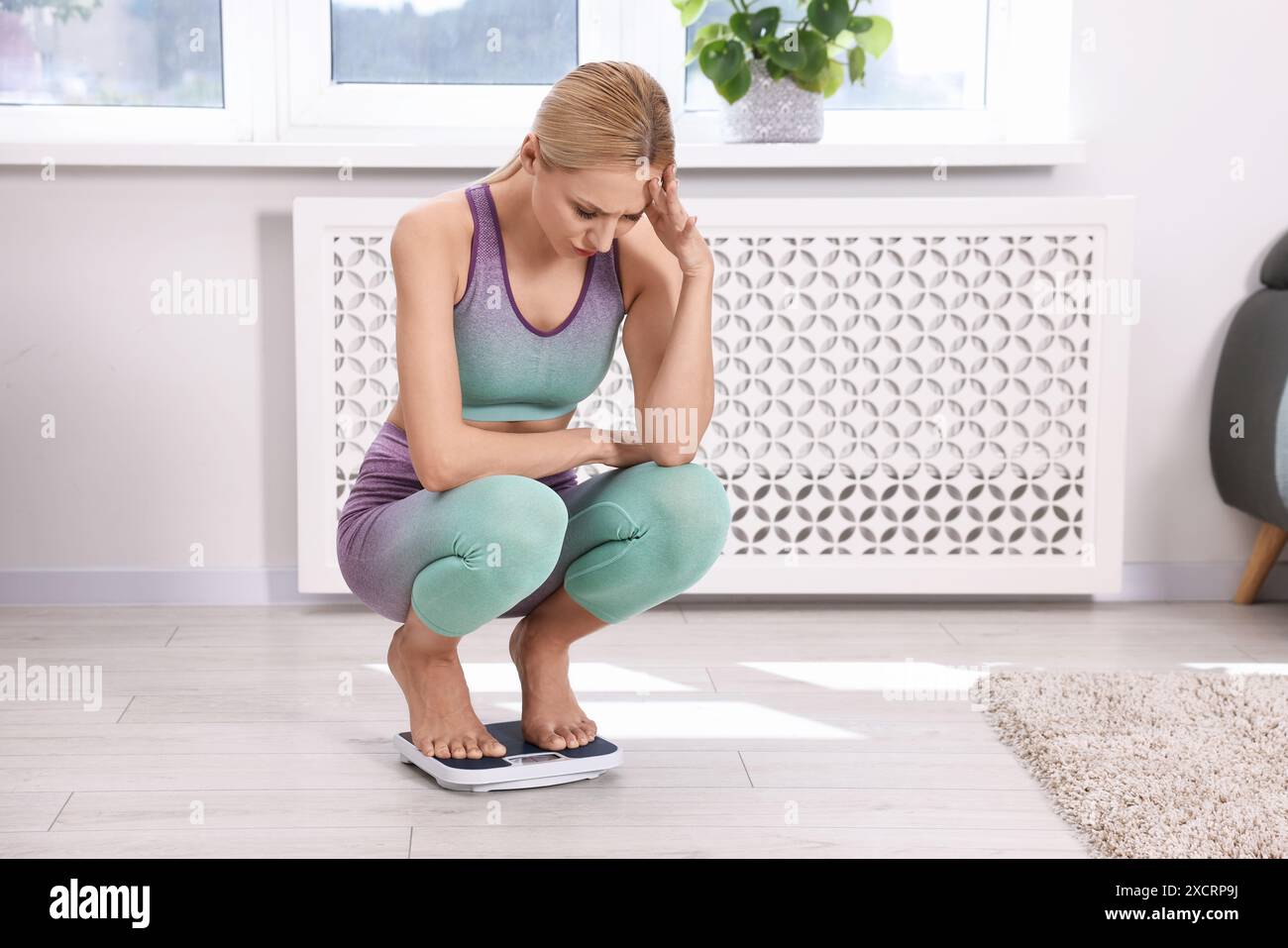 Worried woman on floor scale at home Stock Photo - Alamy