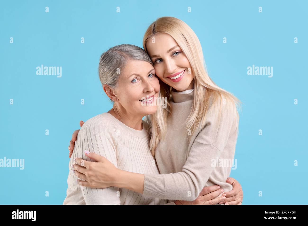Family portrait of young woman and her mother on light blue background ...