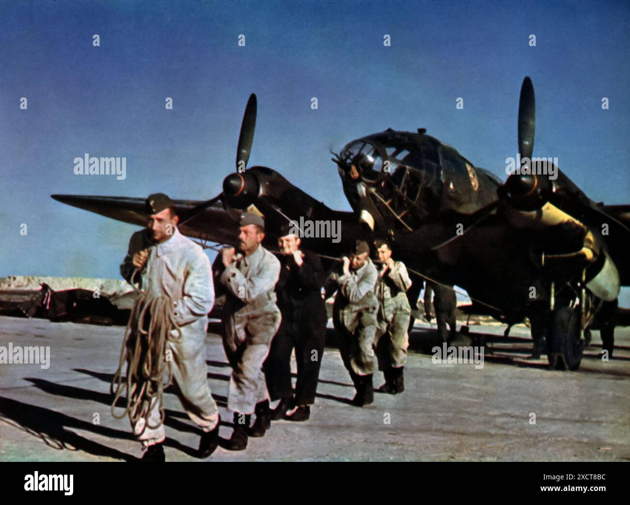 A photograph shows Luftwaffe ground crew members loading a bomb onto an ...