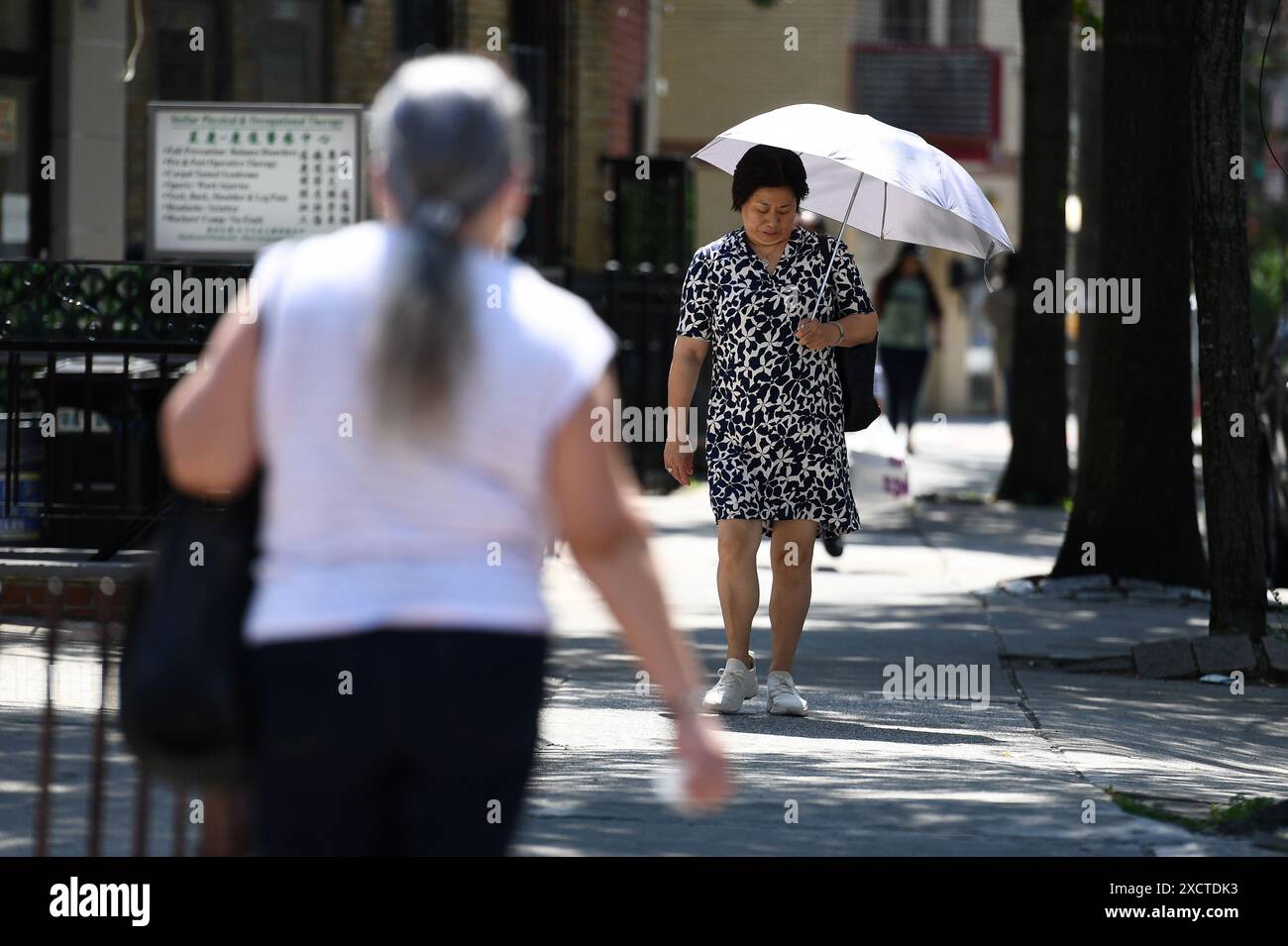 New York, USA. 18th June, 2024. A woman uses an umbrella to shade ...