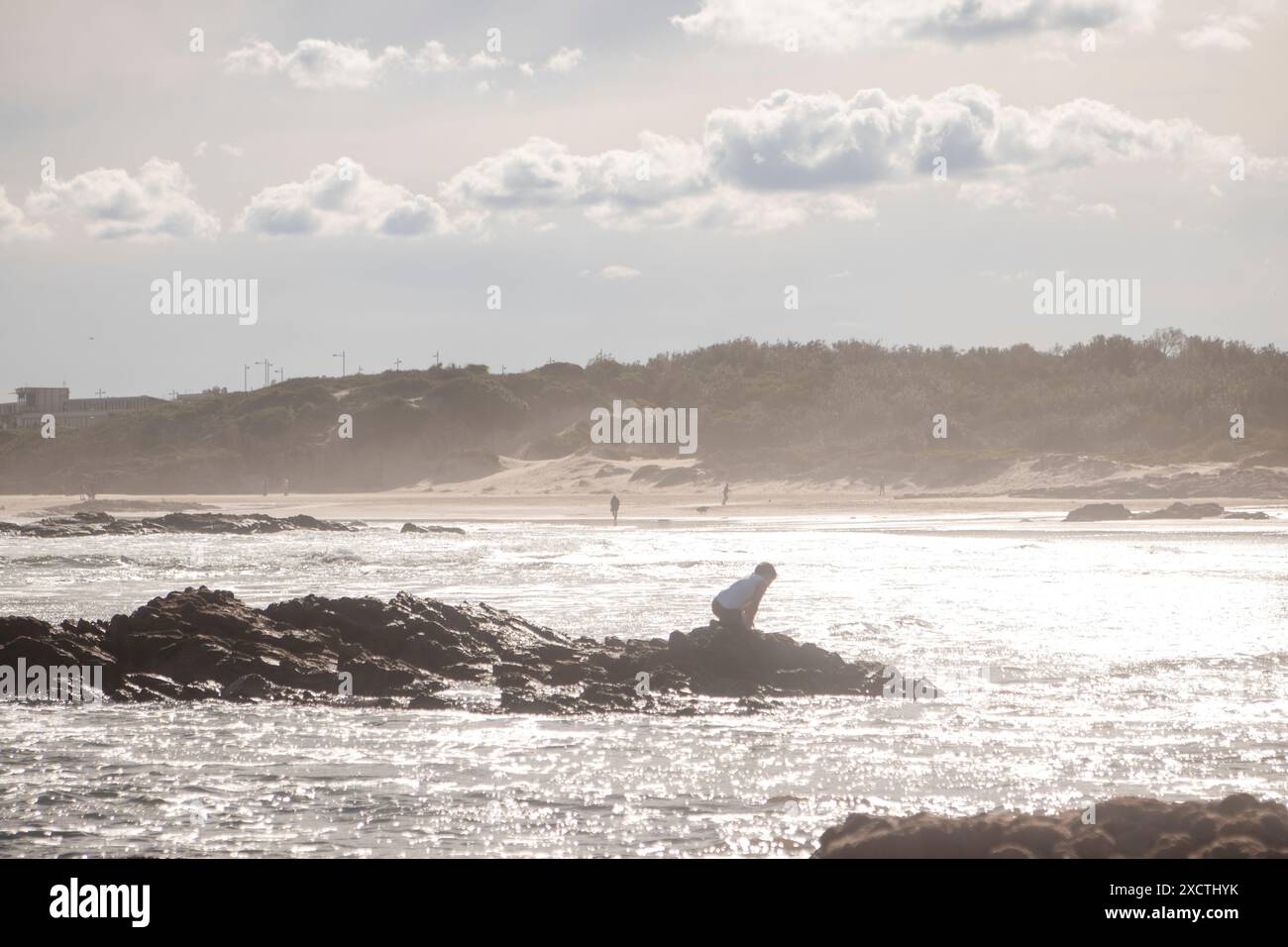 A serene beach scene with a person on rocks and a distant view of the ...
