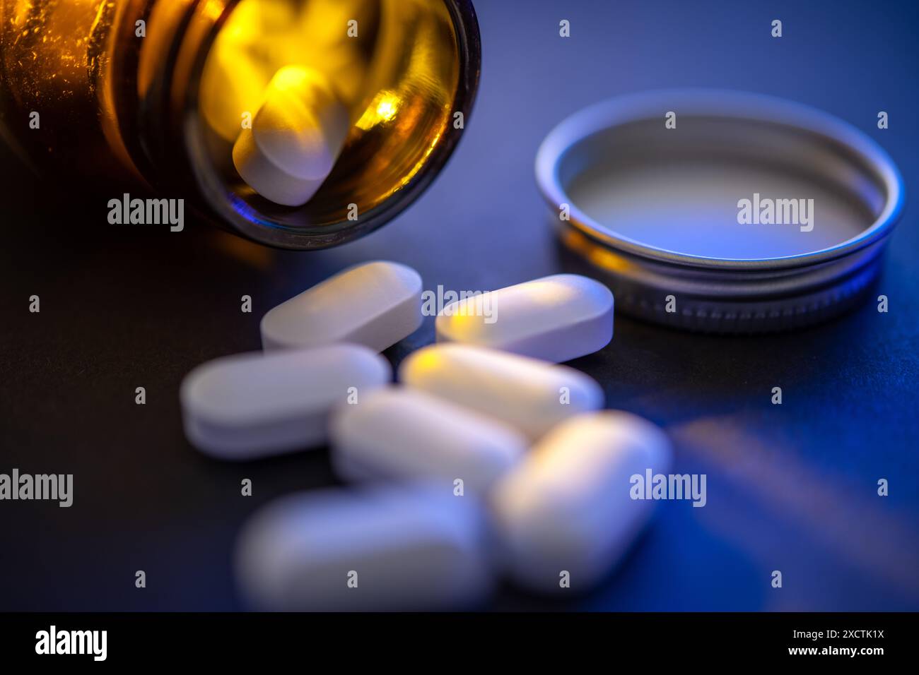 Close-up capture of white pills tumbling out from an amber glass ...