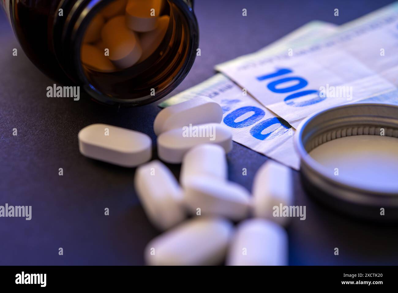 White medication pills spilled from a dark bottle, with 100 Euro ...