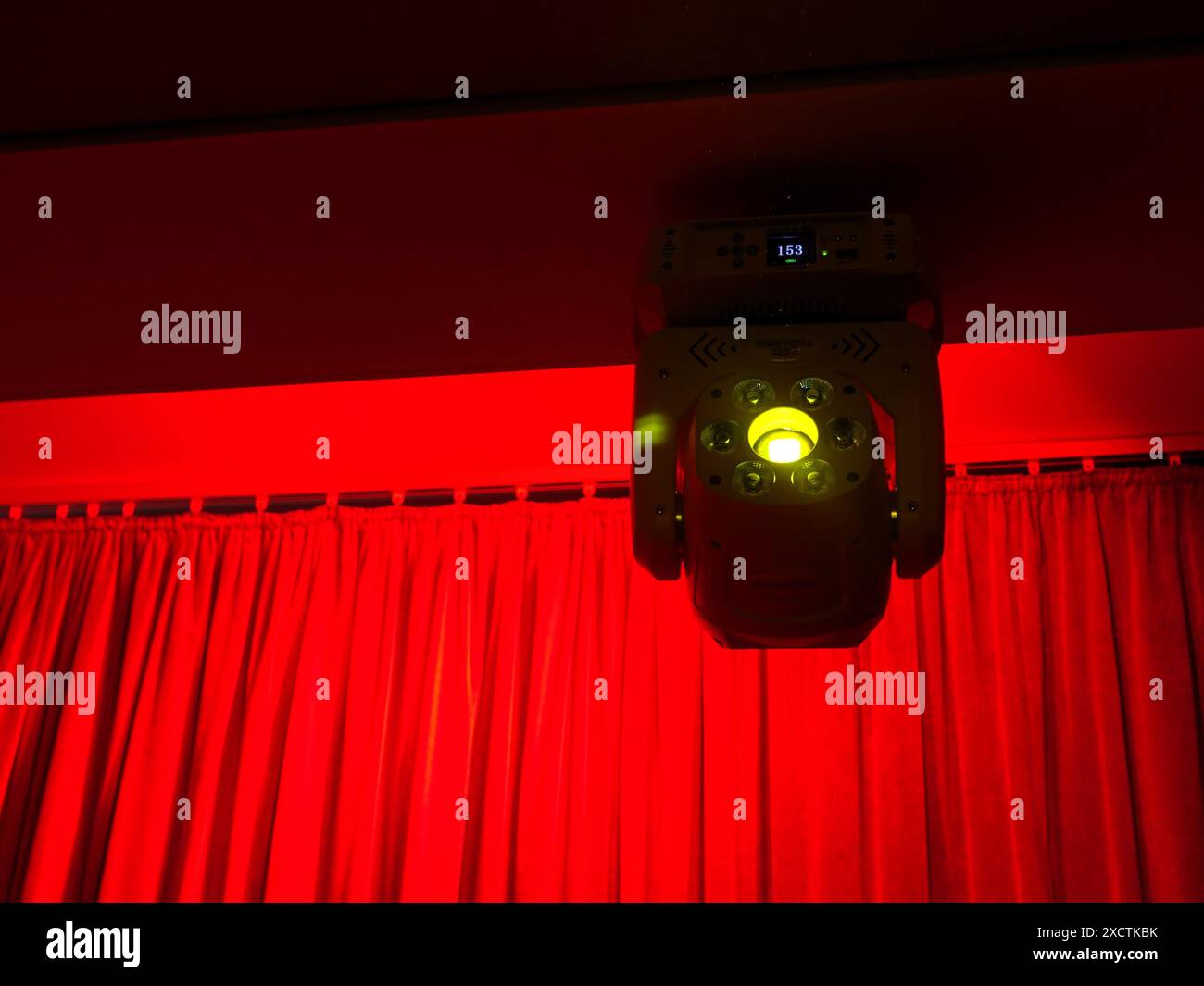 Stage lighting fixture with a red curtain backdrop in a dark theater ...