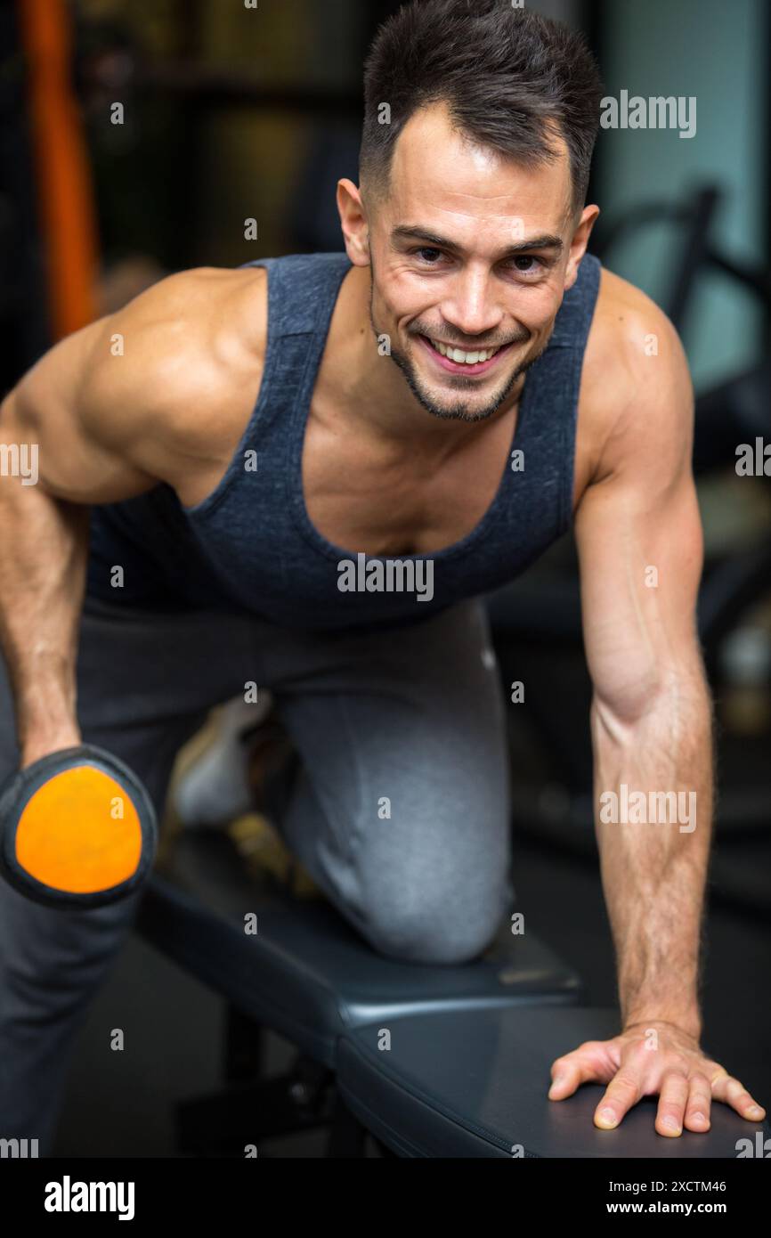 smiling fit man doing one-arm dumbbell rows on bench Stock Photo - Alamy