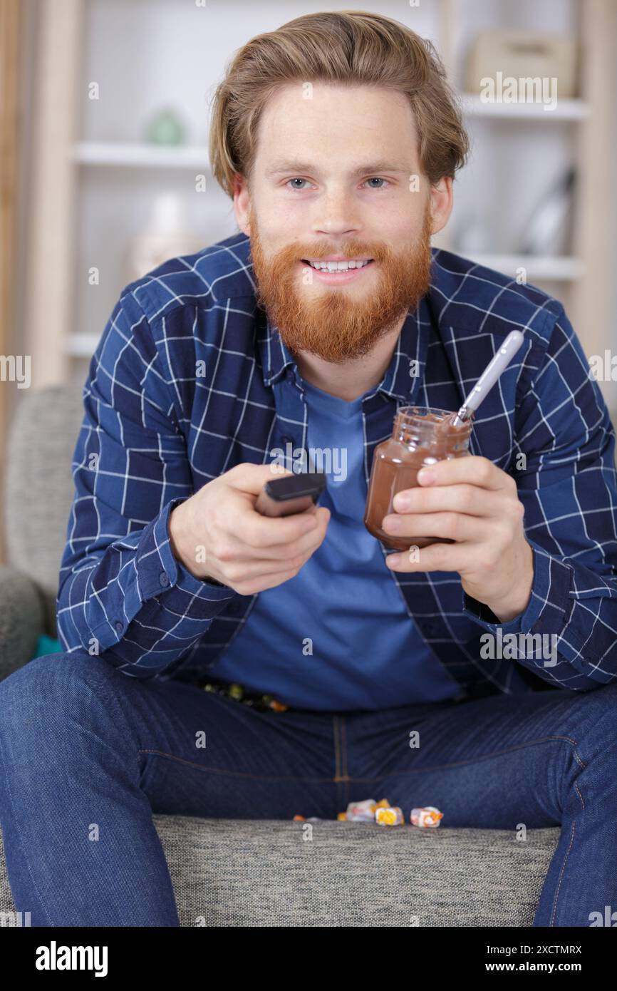 young man eating a chocolate while holding a remote control Stock Photo ...
