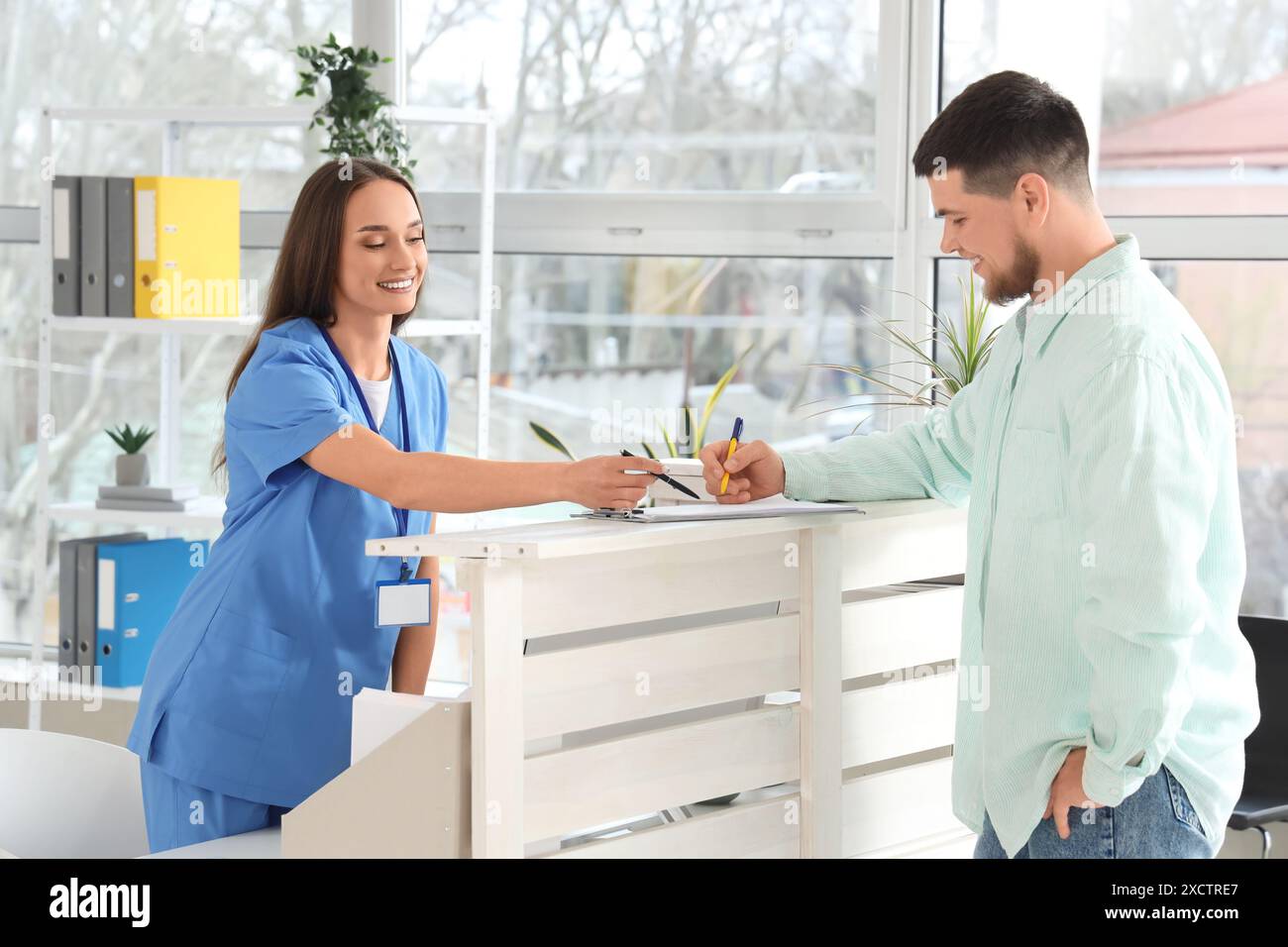 Female receptionist with patient filling out form at desk in clinic ...