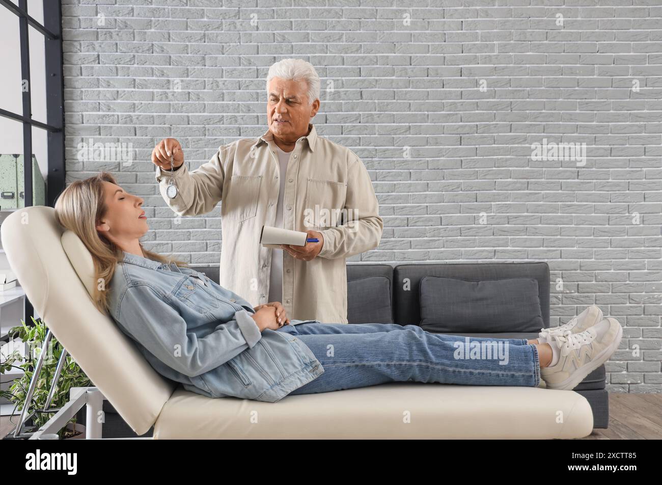 Male psychologist with pocket watch hypnotizing woman in office Stock ...