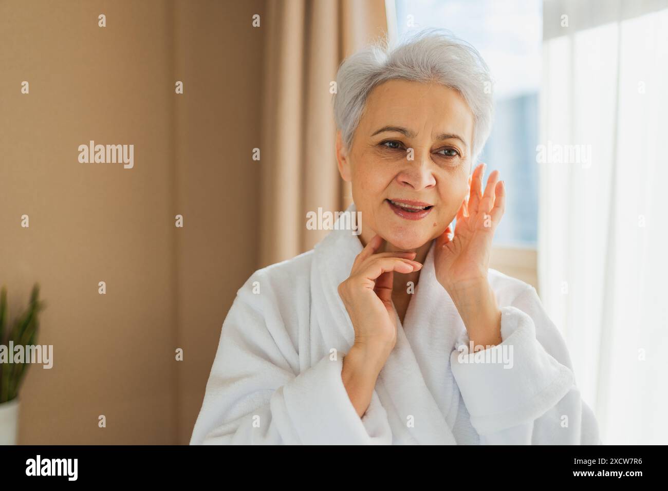 Mature adult old woman applying nourishing anti age face cream doing daily beauty routine ...