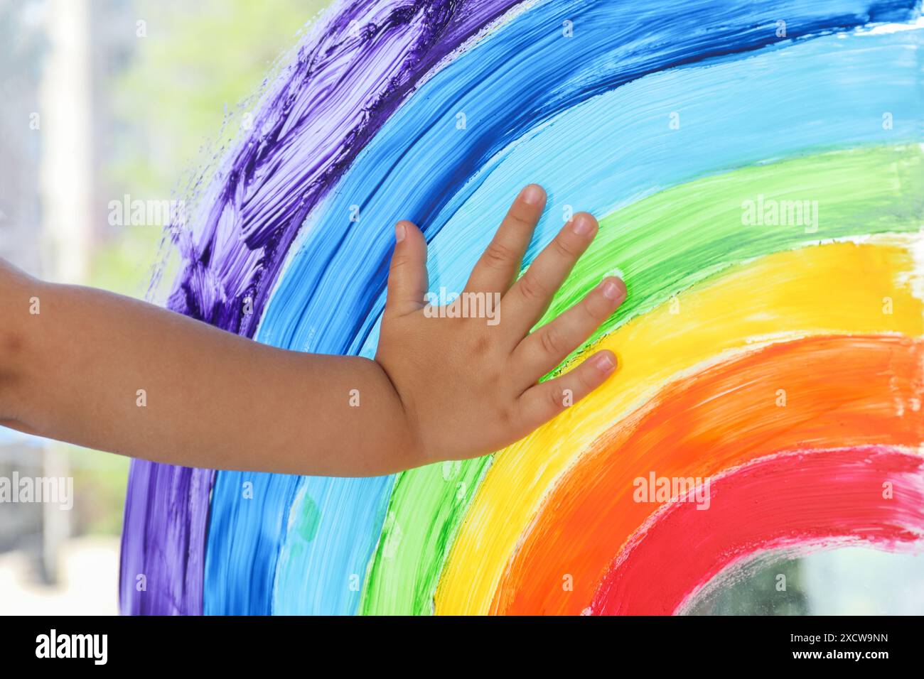 Little girl touching picture of rainbow on window indoors, closeup ...