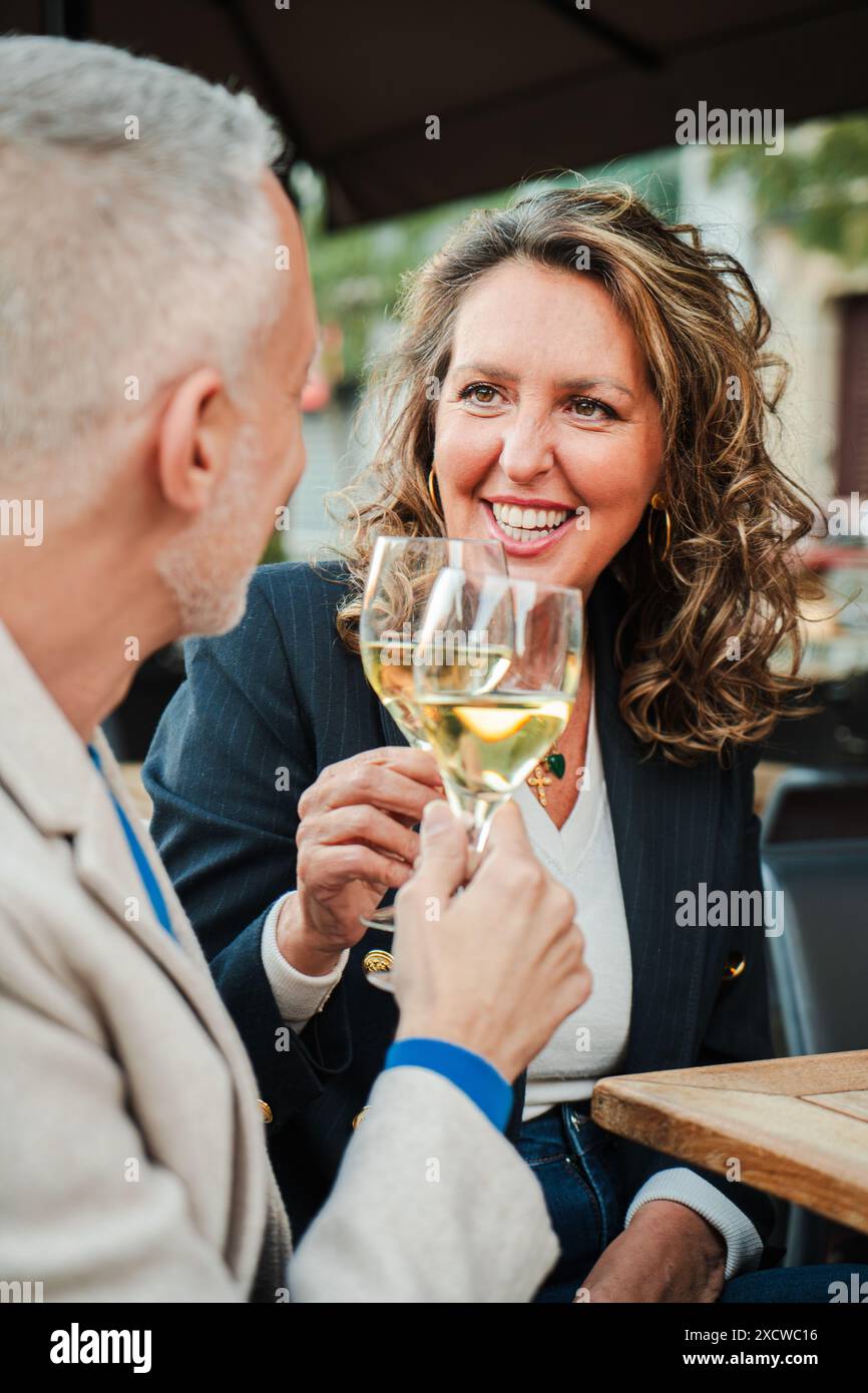 Vertical. Mature couple toasting white wine glasses on a bar terrace ...