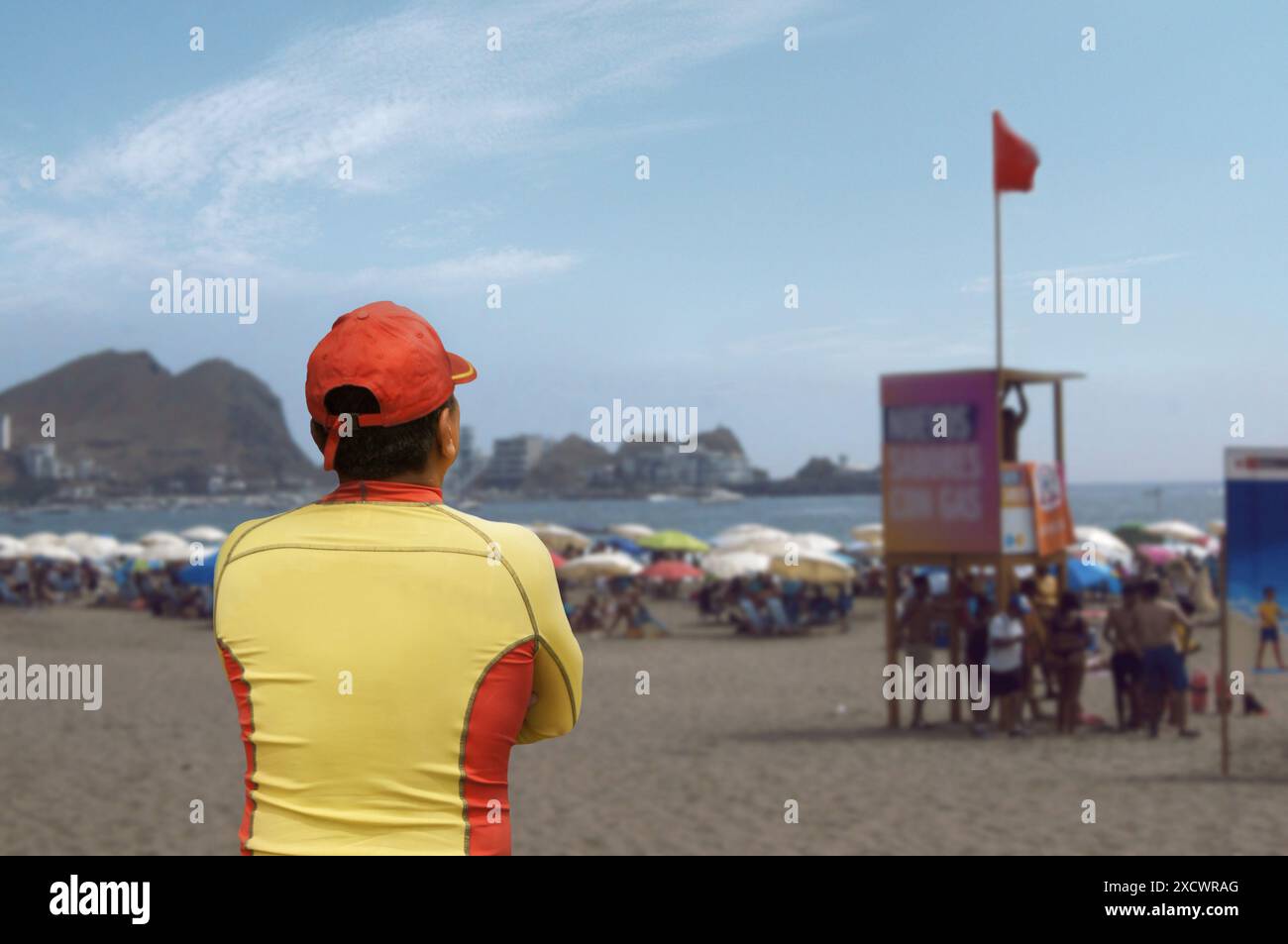 Lifeguard in yellow and red t-shirt on the beach with the watchtower in ...