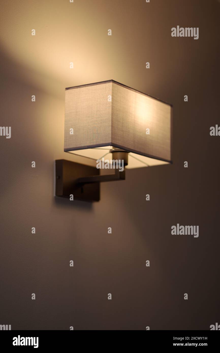 An elegantly simple wall-mounted lamp illuminates with a soft ...