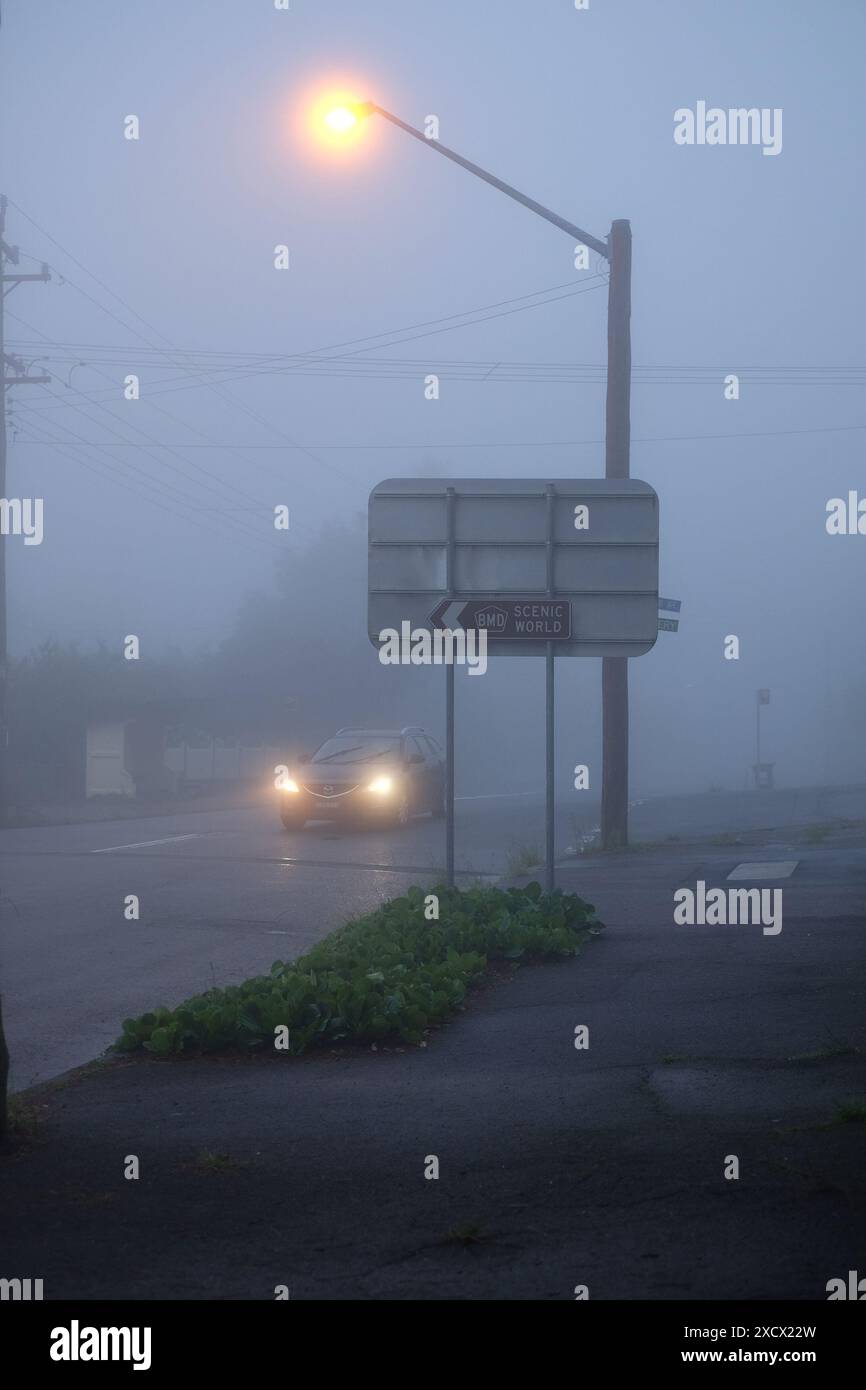 A car drives under a glowing streetlight and power lines in heavy fog ...