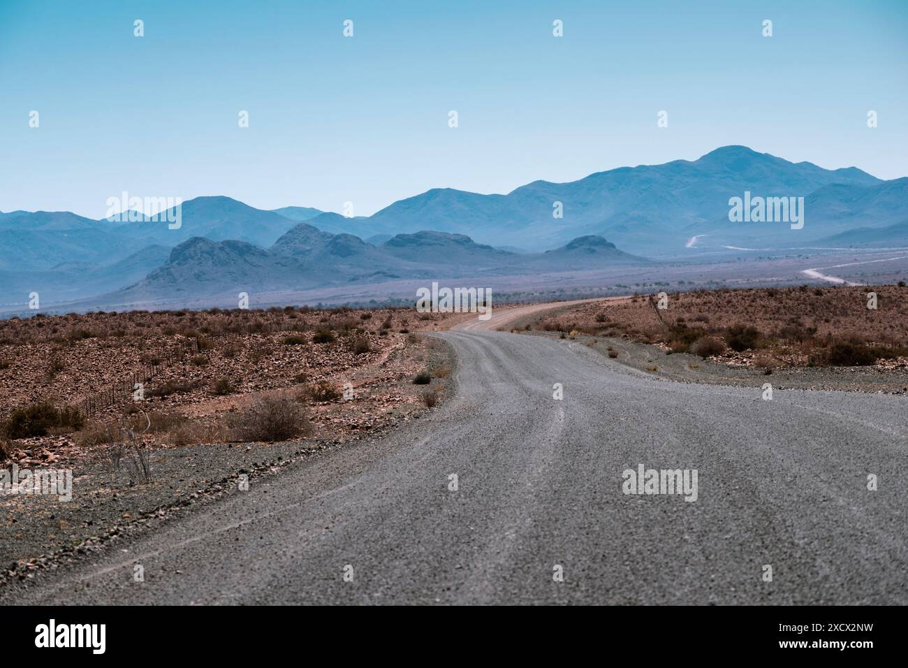 gravel road in desert leading towards mountains in blue evening haze ...