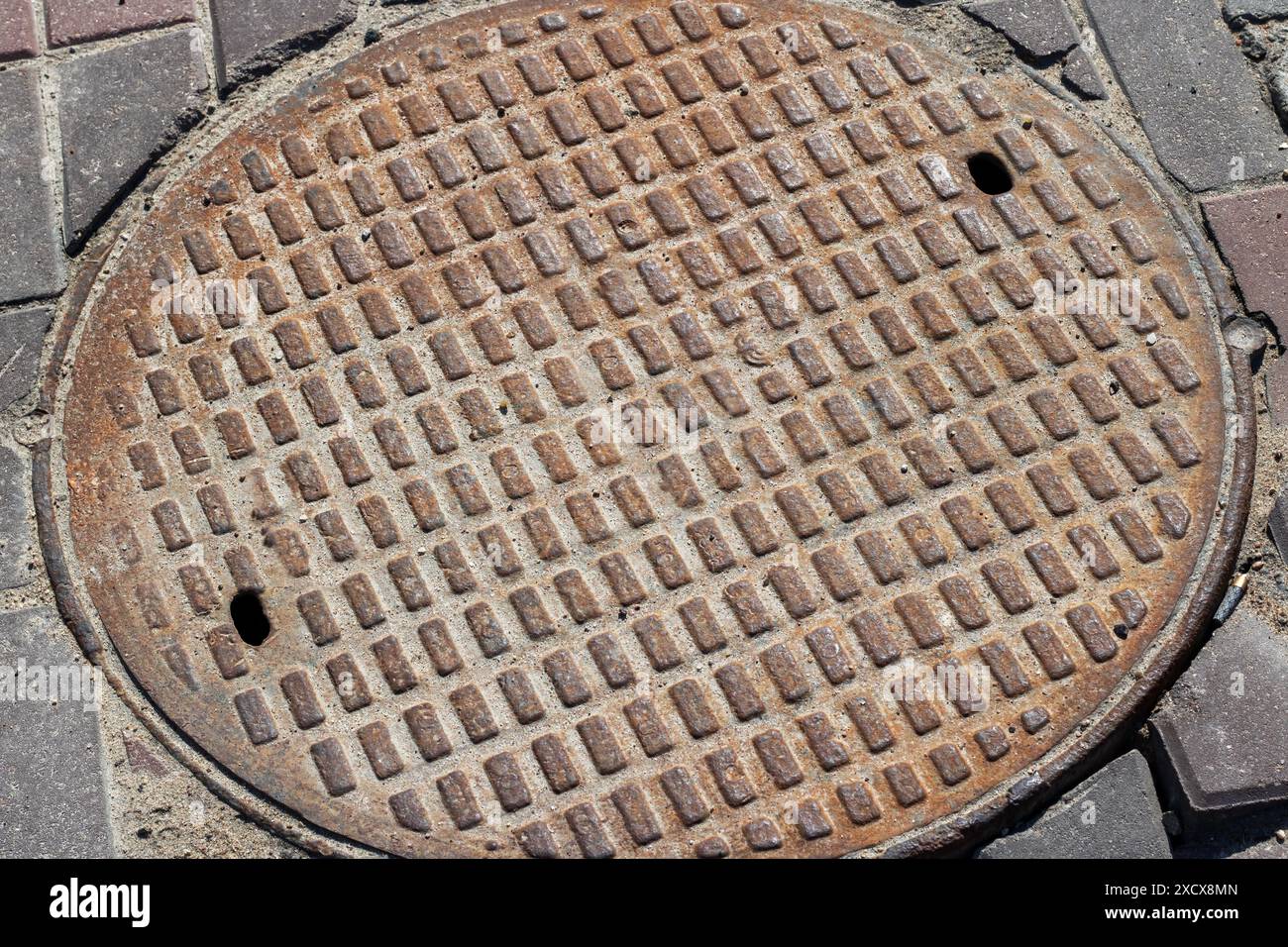 A round manhole cover is placed on a sidewalk made of bricks ...