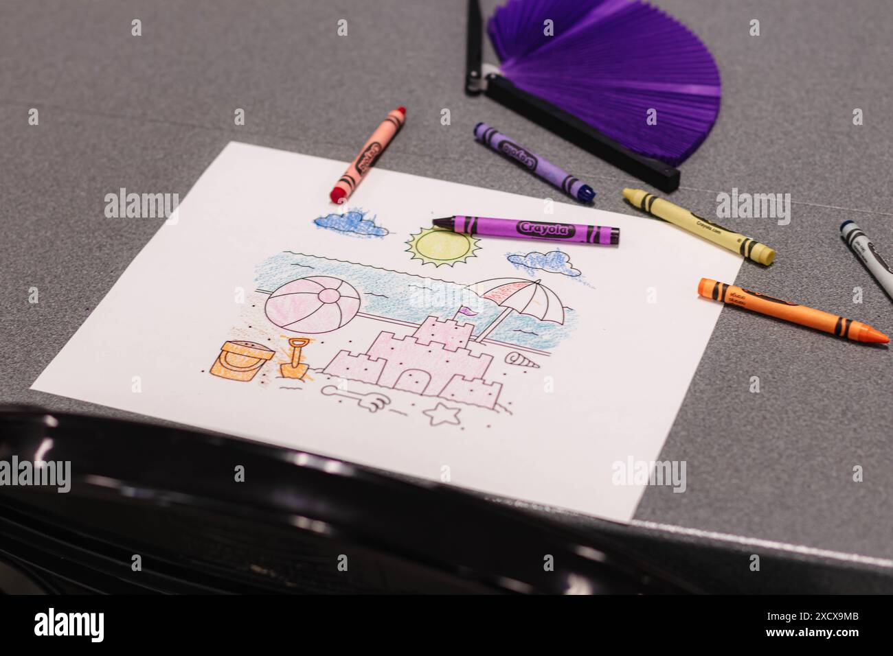 A colorful drawing of a beach scene with crayons scattered on a table ...