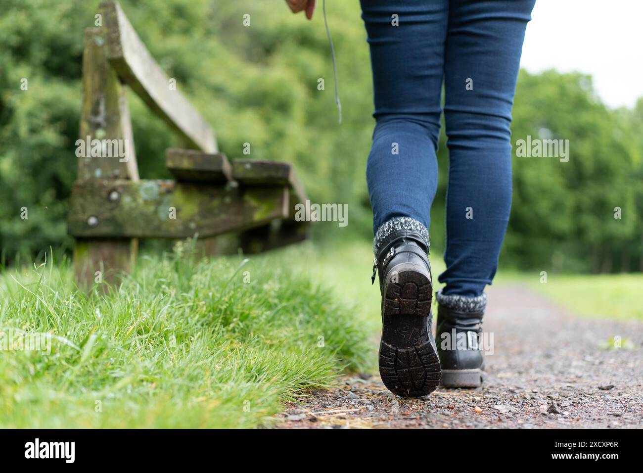Rear low point of view of a woman in jeans & boots walking in a UK park ...