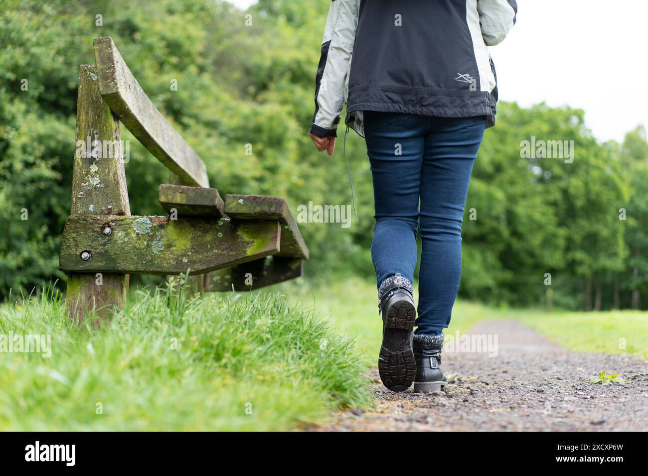 Rear low point of view of a woman in jeans & boots walking in a UK park ...