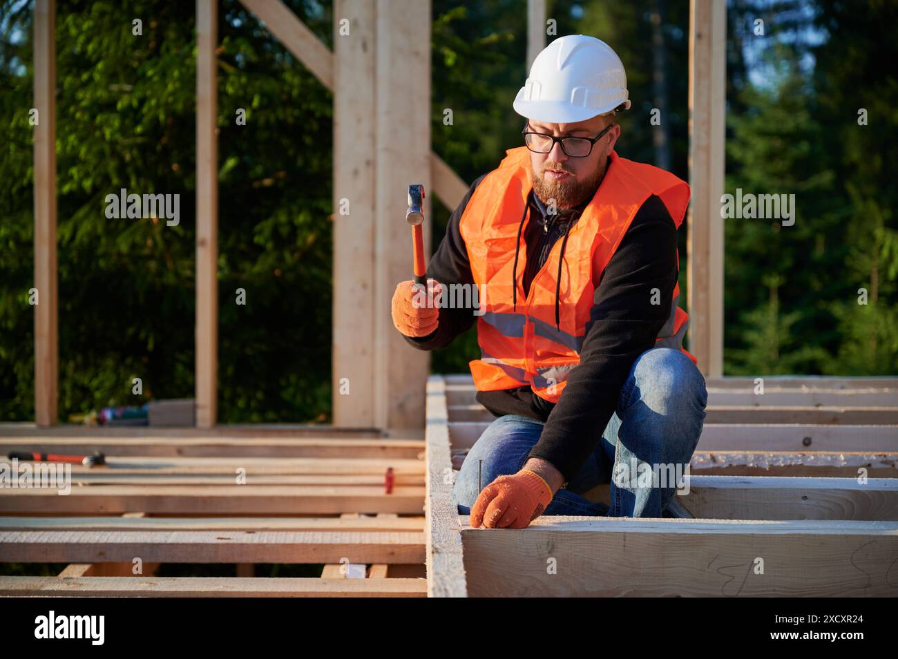Wooden frame, two-story abode is being built by carpenter near forest ...