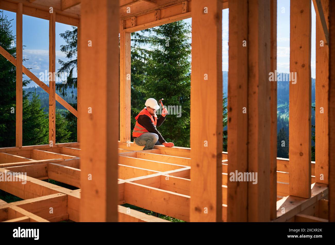 Carpenter constructing two-story wooden frame house near forest. Man ...